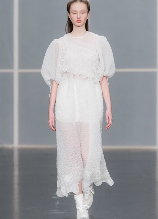 Cecilie Bahnsen's FW20 collection showcases an ethereal white midi dress with textured fabric and voluminous sleeves, paired with sporty footwear