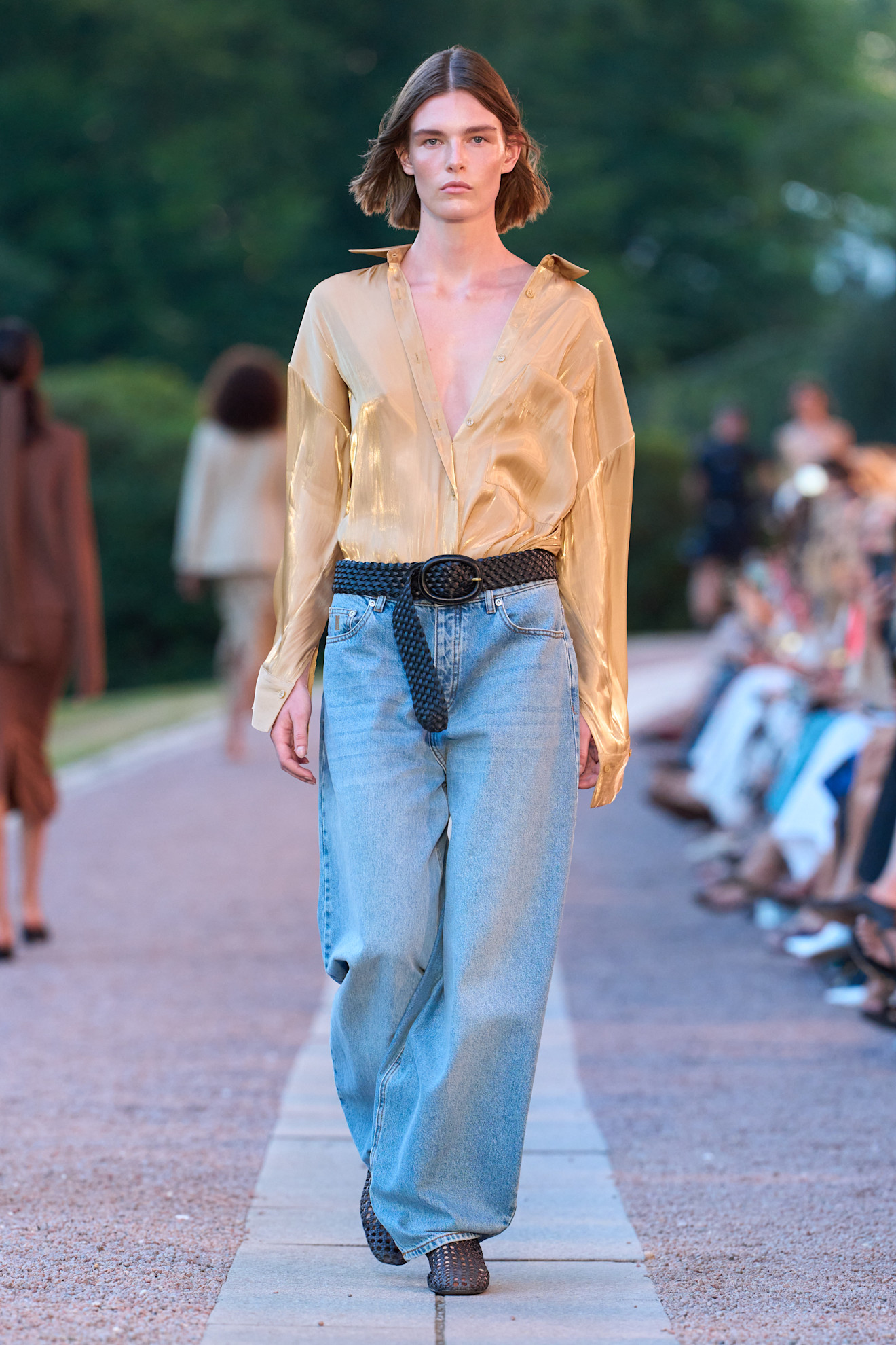 Malene Birger spring summer 2027 outfit featuring a gold satin blouse with deep V-neck and wide-leg light blue jeans with a black woven belt