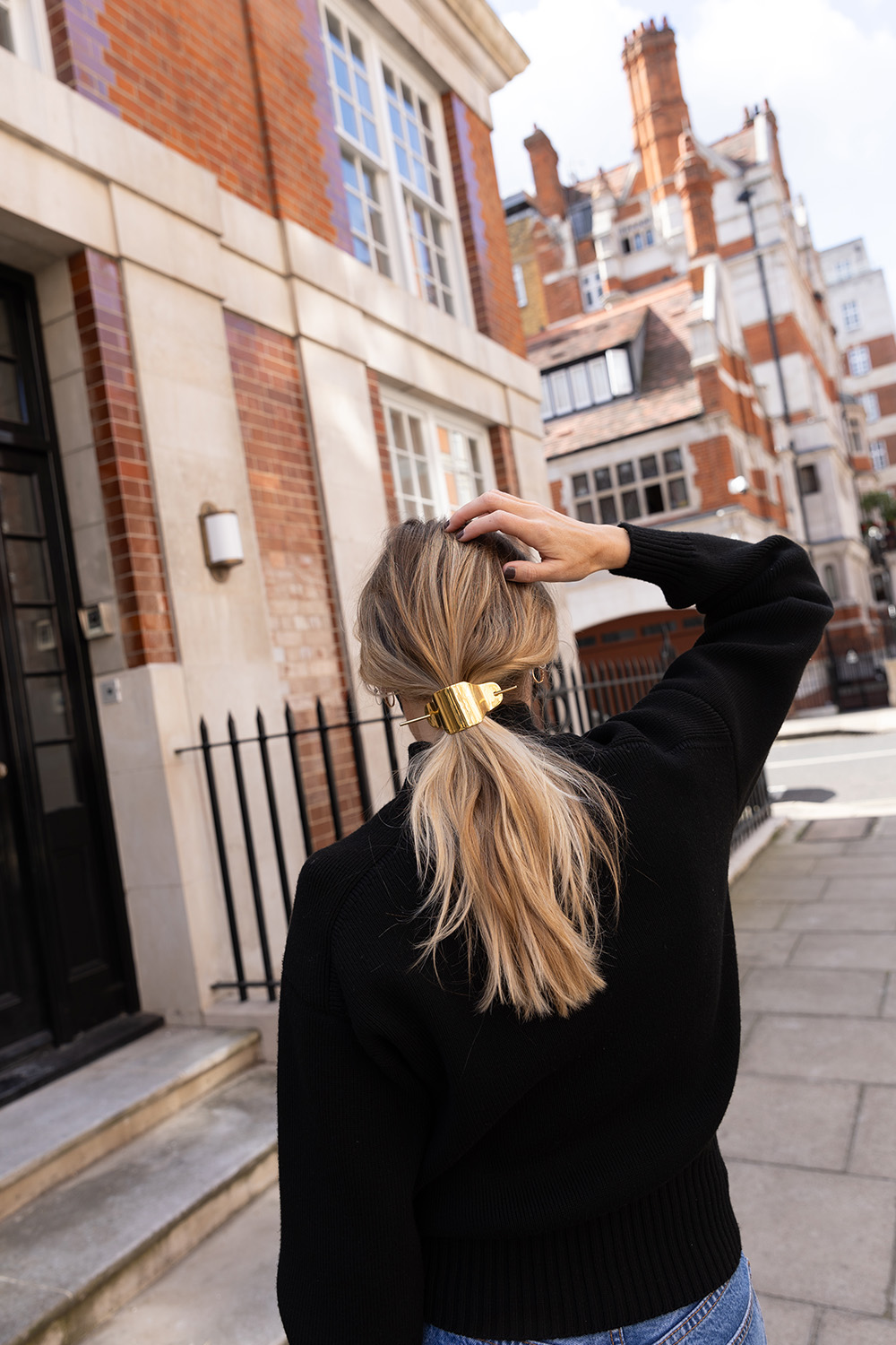 Trendy gold hair clip styled in a casual ponytail%2C worn by a woman in a cozy black sweater against a chic urban backdrop