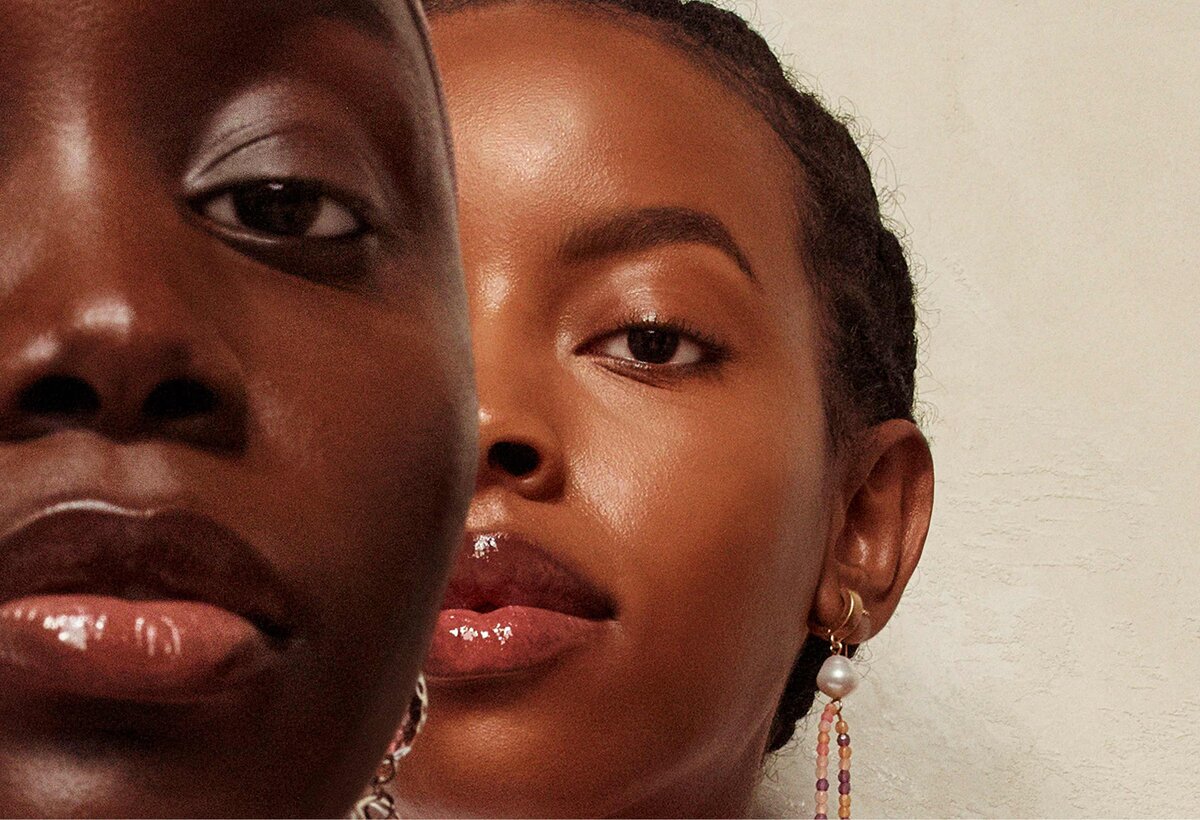 Close-up of two women showcasing glossy lips and radiant skin%2C featuring elegant hoop earrings with pearls and colorful beads