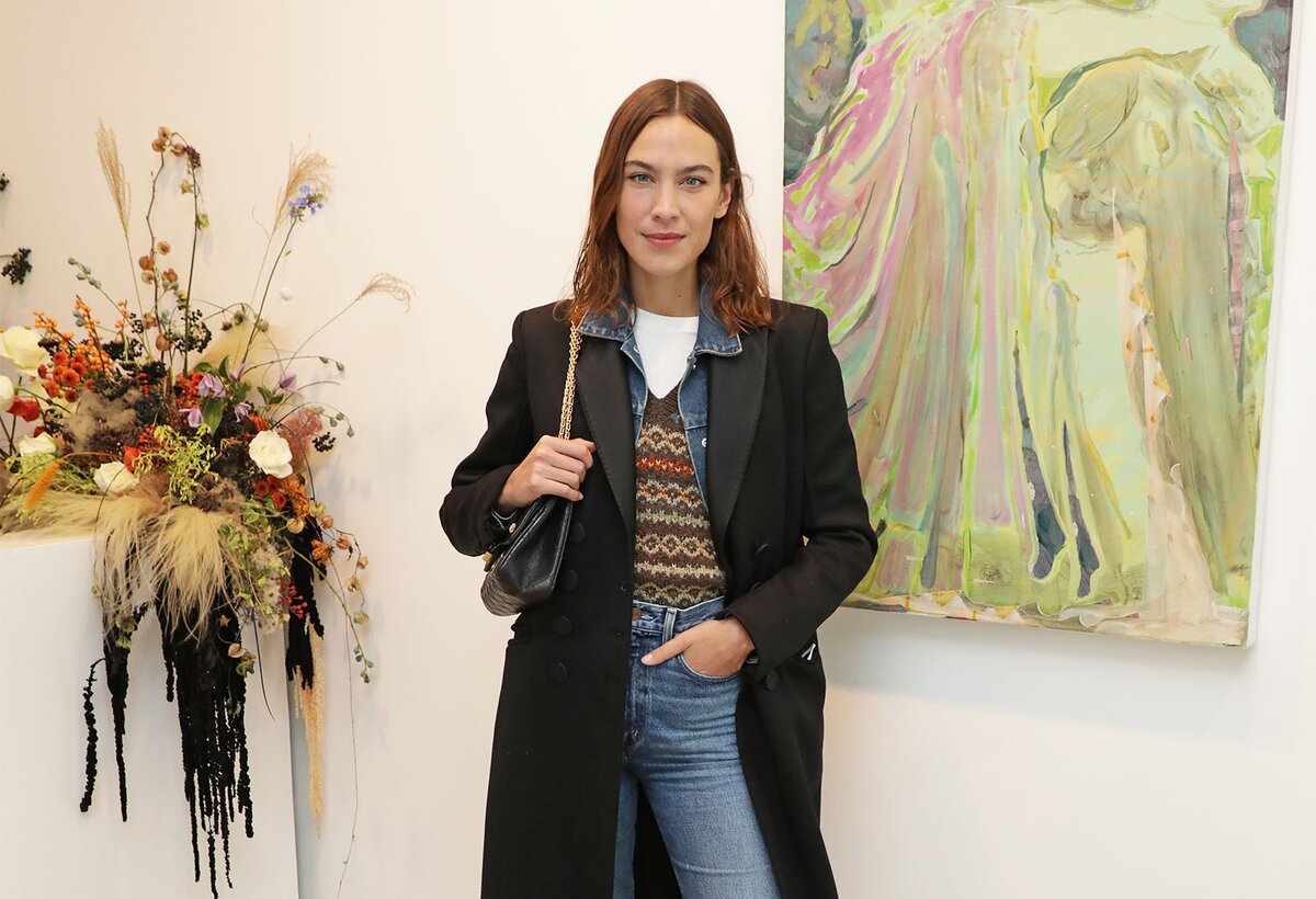 Alexa Chung showcases an effortlessly chic outfit featuring a tailored black coat over a patterned sweater%2C paired with high-waisted jeans and a sleek black handbag
