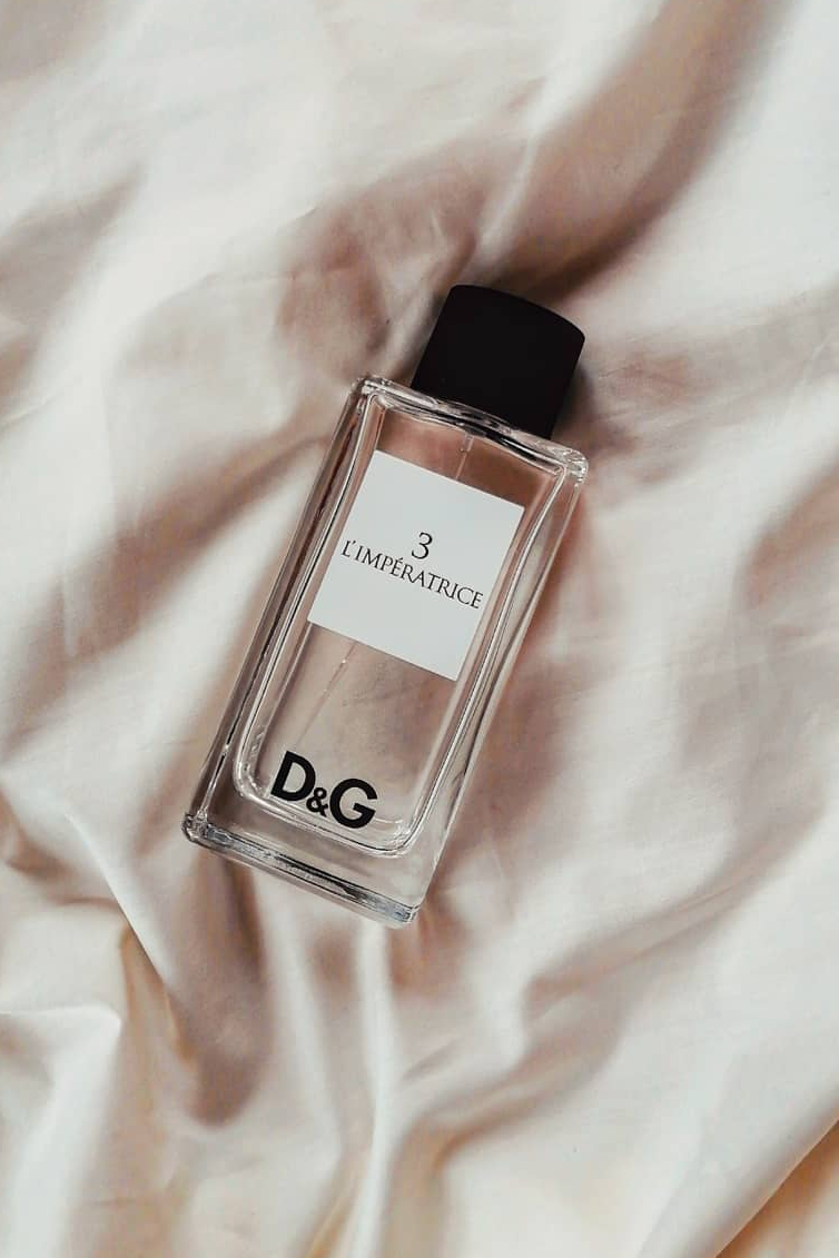 Dolce %26 Gabbana L%27Imperatrice fragrance bottle displayed on soft%2C beige fabric%2C featuring a sleek rectangular design with a black cap and label