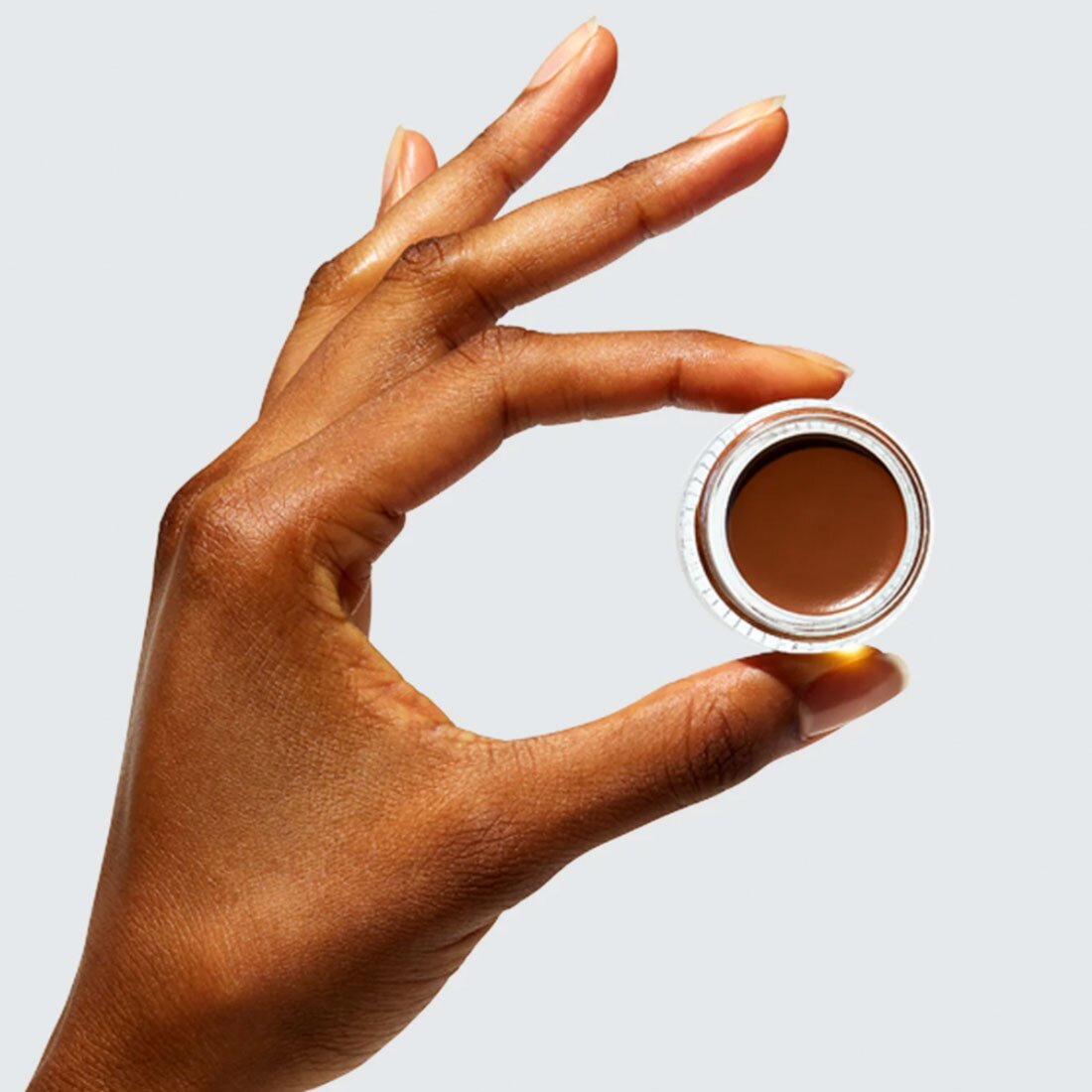 A woman's hand is holding a cream concealer tub.