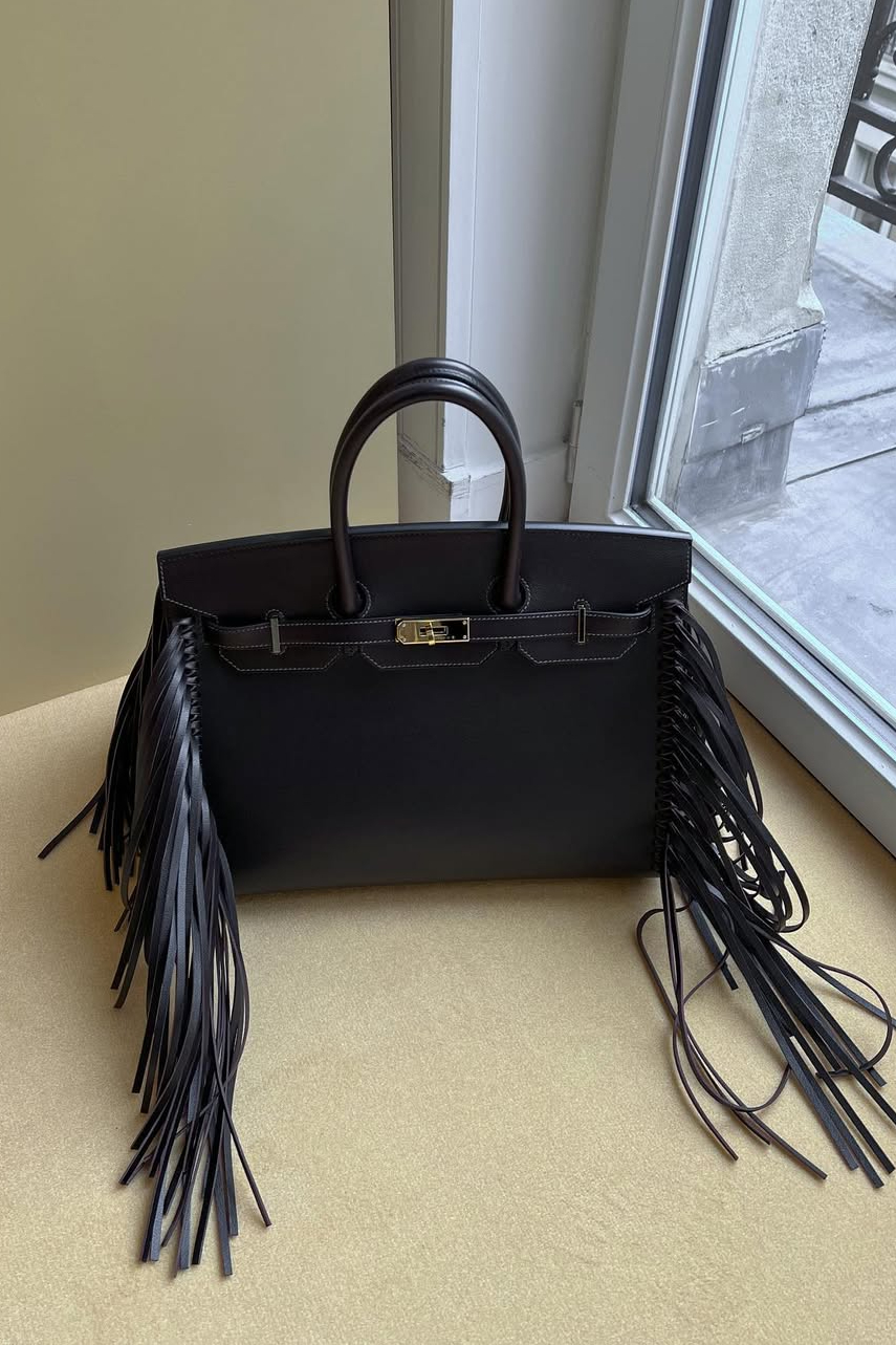 Black leather fringe handbag with top handles and gold hardware%2C styled on a windowsill in a minimalist interior setting