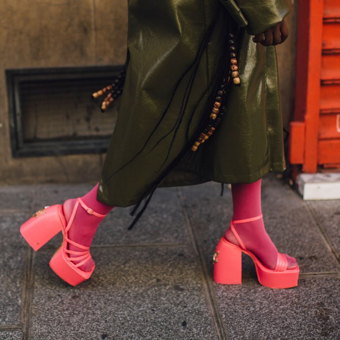 A woman standing on streets in pink block heels. 