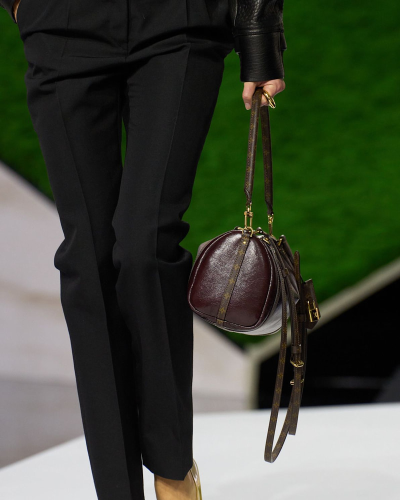 Black tailored trousers paired with a textured black leather jacket and a burgundy Louis Vuitton leather handbag with monogram straps