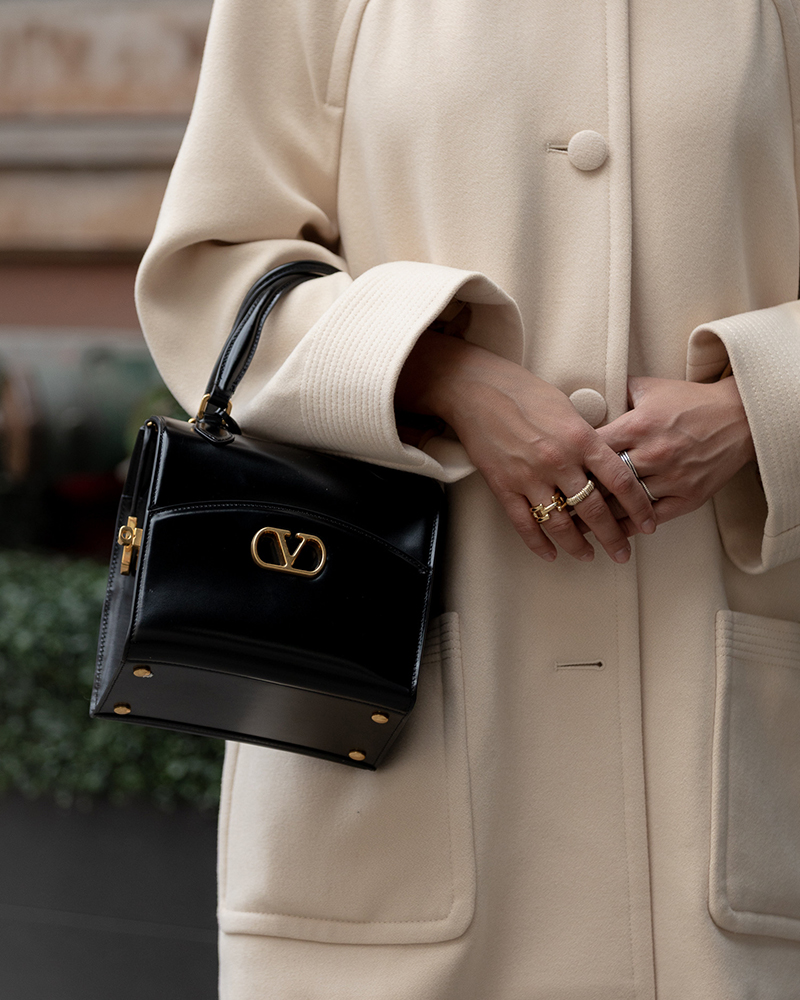 Valentino Garavani black leather bucket bag with gold VLogo hardware styled against a cream wool coat for refined winter street style