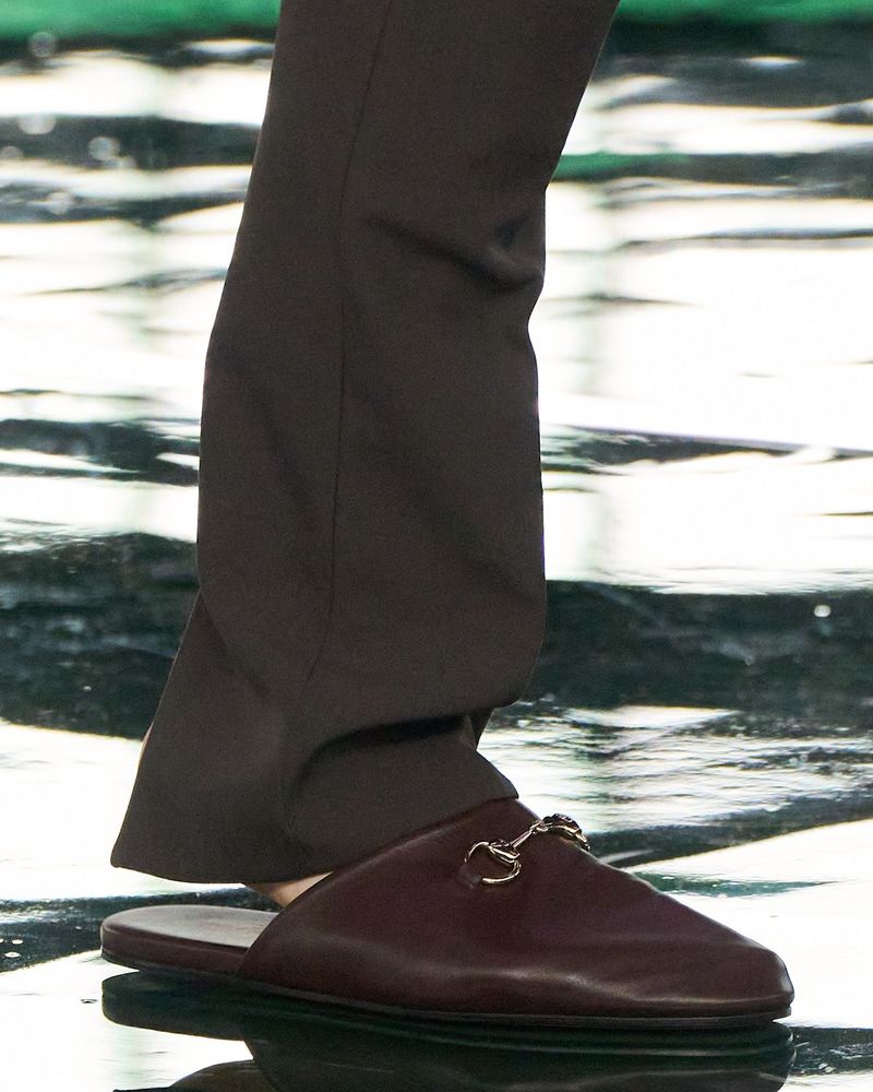 Gucci men%27s brown leather horsebit mule slippers paired with tailored dark brown trousers on runway