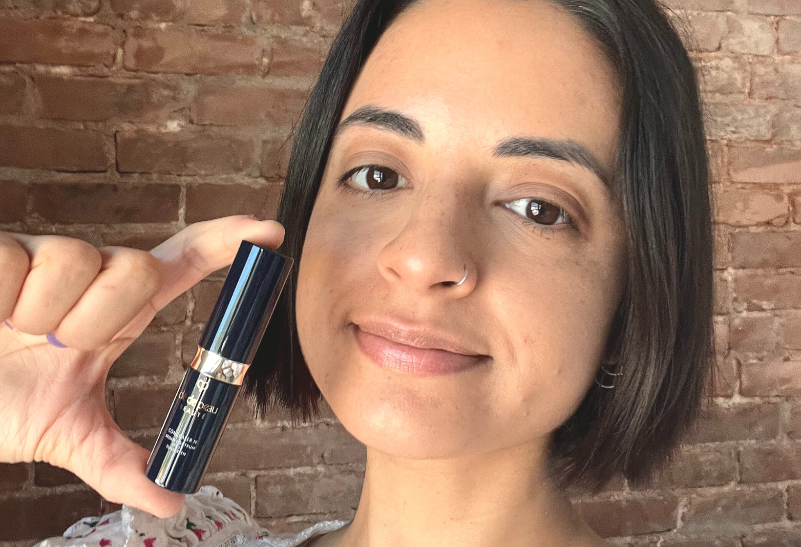 Cl%C3%A9 de Peau Beaut%C3%A9 concealer stick in black and gold tube held beside face with natural makeup and short dark bob haircut