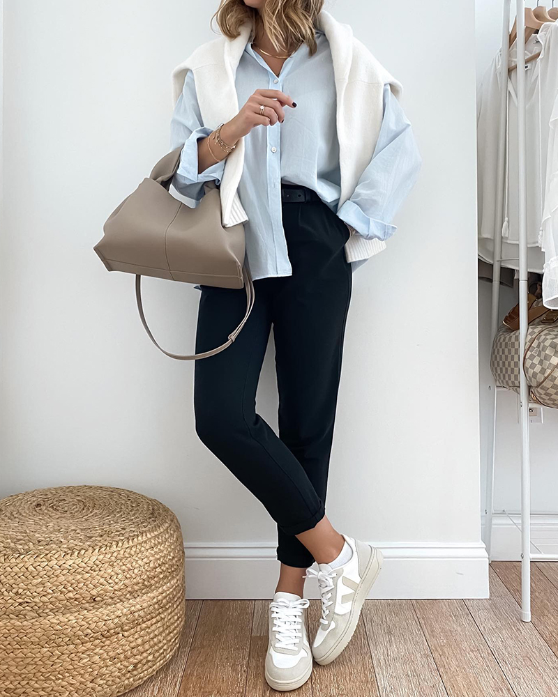 Veja white leather sneakers paired with black trousers%2C blue shirt and taupe shoulder bag in a minimalist indoor setting