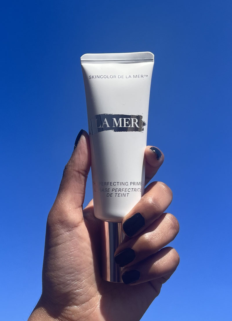 Hand holding La Mer’s The Perfecting Primer against a sky backdrop