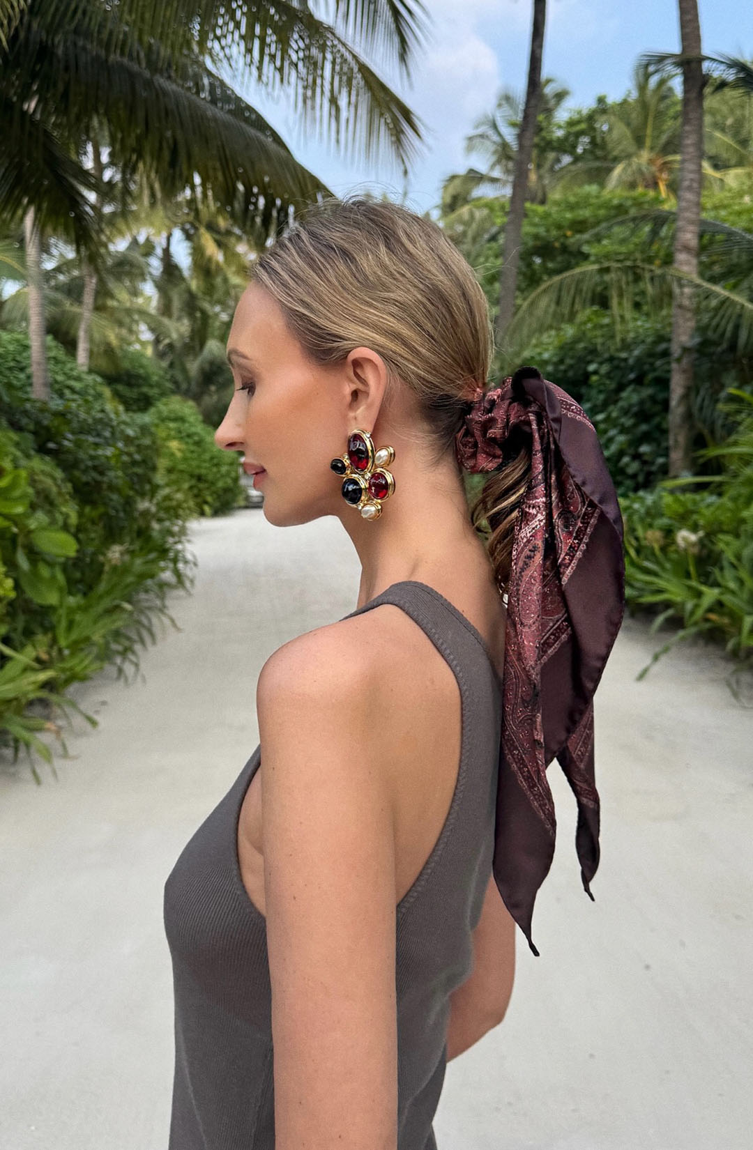 Chic summer look featuring a brown ribbed tank top%2C paired with a patterned silk scarf hair accessory and bold gemstone earrings