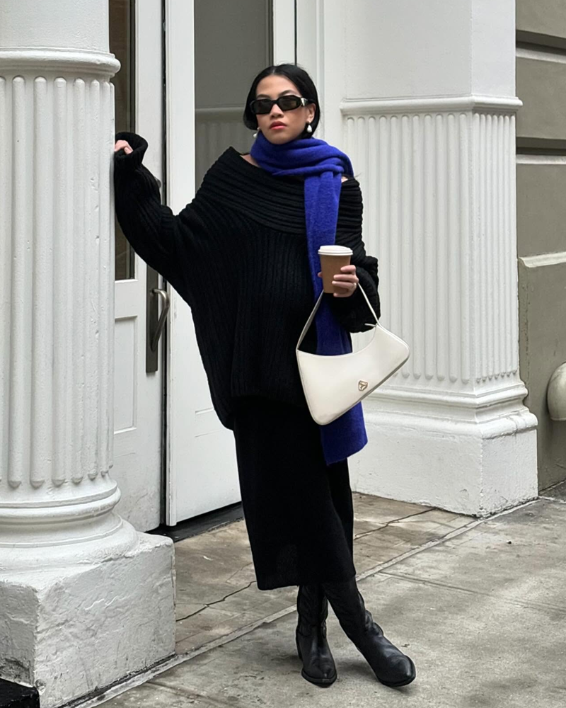 Black knit sweater and midi skirt styled with a cobalt blue scarf%2C white shoulder bag and black boots on a city sidewalk