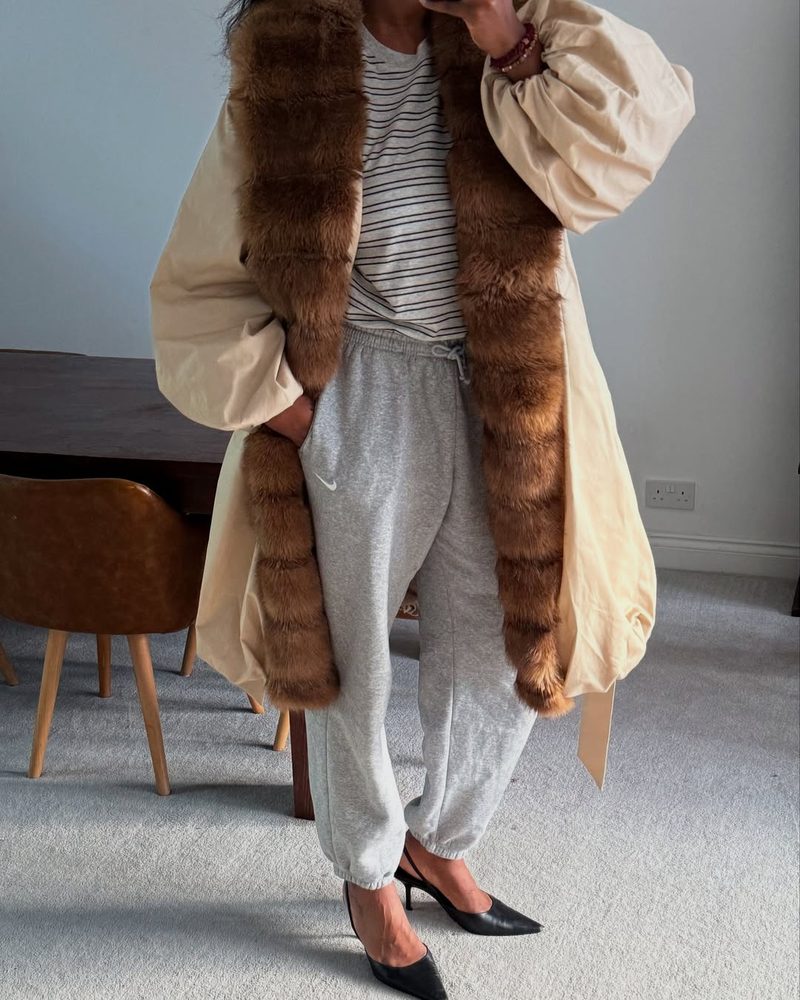 Sporty chic look featuring grey Nike sweatpants paired with a striped tee and a luxurious cream puffer coat with faux fur trim%2C complemented by black stilettos.