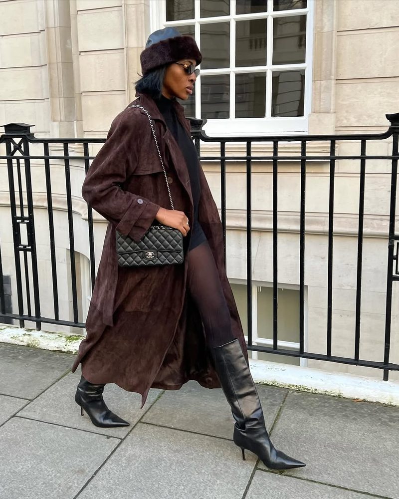 Sleek winter ensemble featuring a deep brown suede trench coat%2C fitted black turtleneck%2C high-heeled black boots%2C and a classic Chanel quilted bag