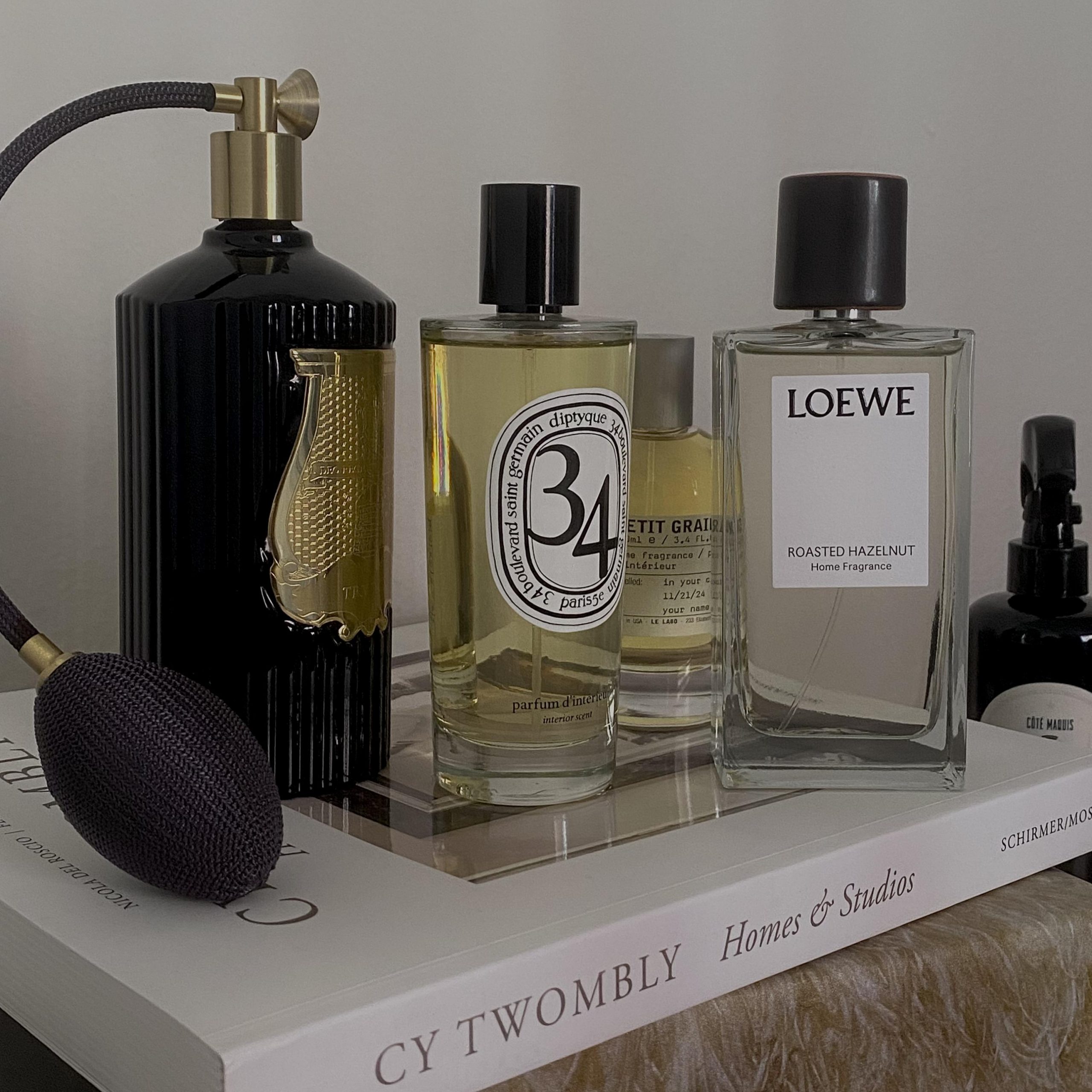 Diptyque 34 interior fragrance bottle alongside Loewe roasted hazelnut scent%2C elegantly displayed with a vintage perfume atomizer on a table