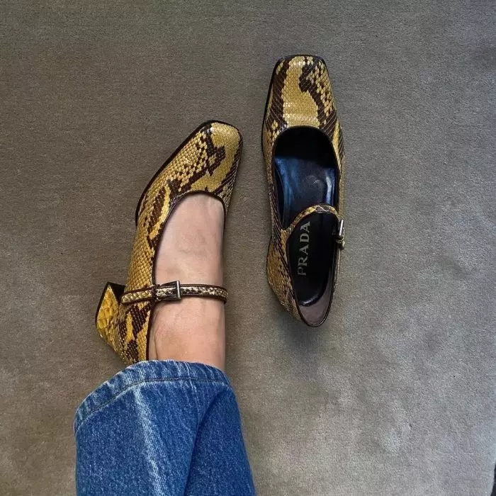 Prada's striking yellow and brown snake print Mary Jane heels feature a chic ankle strap and square toe, styled with casual denim.