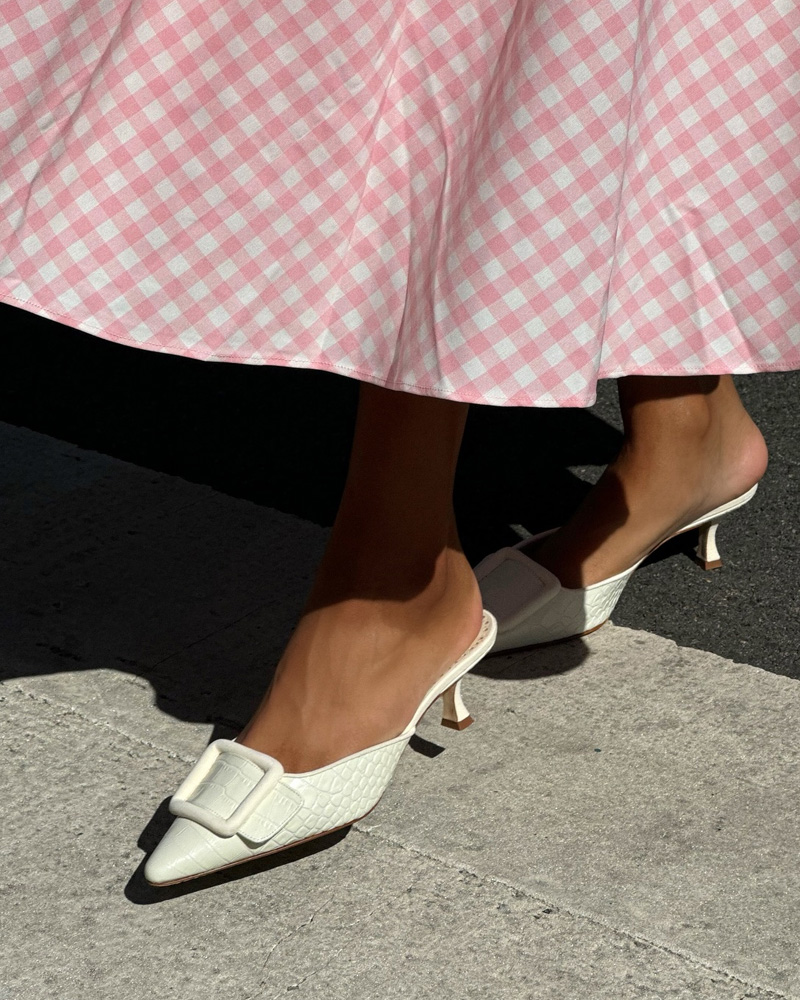 White crocodile-embossed leather kitten heel mules with a large buckle detail paired with a pink gingham midi skirt on sunlit pavement