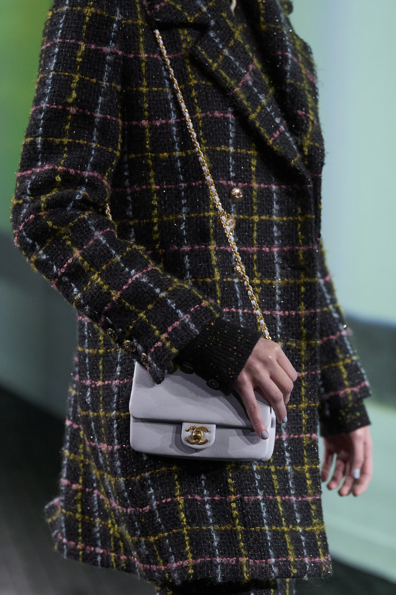 Black tweed Chanel coat with yellow and pink plaid pattern paired with a light gray leather Chanel flap bag with gold chain strap