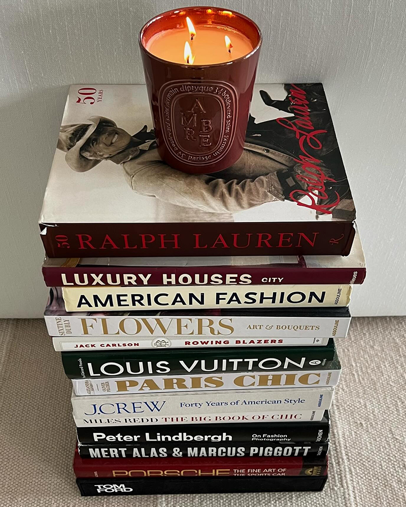 Stack of luxury fashion books with Diptyque amber candle on top%2C including Ralph Lauren and Louis Vuitton titles