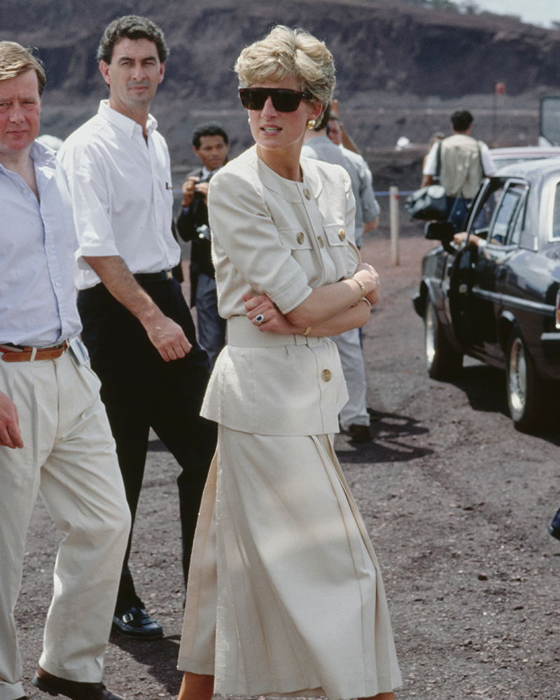 Cream skirt suit with oversized black sunglasses and pumps%2C styled outdoors near parked cars