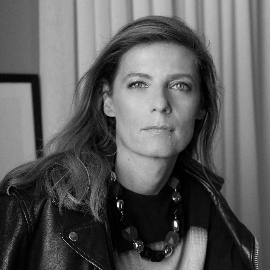 A woman in a leather jacket, graphic tee, and blue jeans poses for a camera.