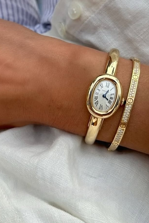 Elegant Cartier Love bracelet alongside a gold watch with a white face and Roman numerals%2C set against a soft%2C textured background
