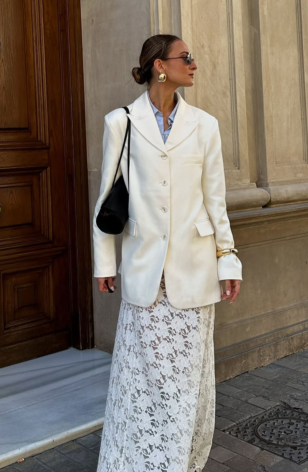 Chic spring outfit featuring an oversized white blazer%2C lace maxi skirt%2C and a black handbag%2C styled with a light blue blouse and statement earrings