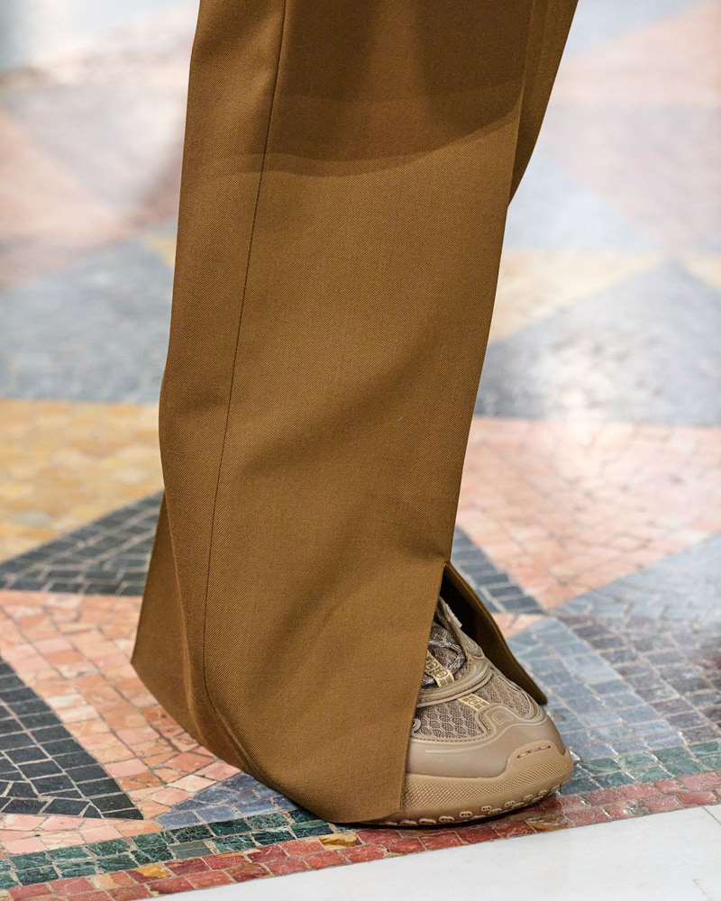 Brown wide-leg trousers paired with beige Gucci mesh and leather sneakers on mosaic floor