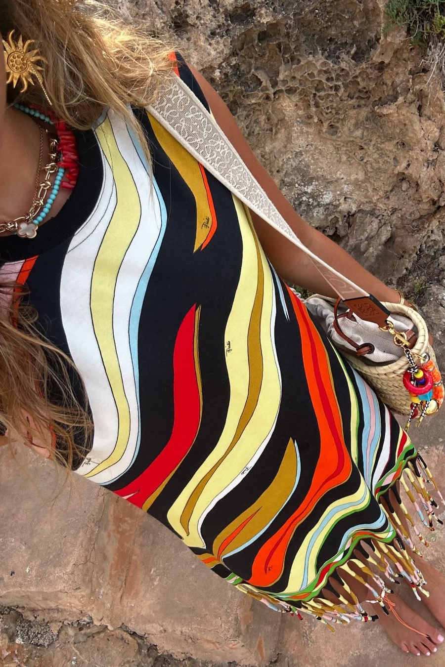 Colorful beach dress with wavy patterns in red%2C yellow%2C and black%2C paired with a straw bag and layered jewelry for a chic coastal look