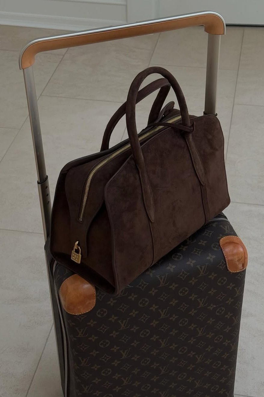Dark brown suede weekender bag by Louis Vuitton elegantly perched on top of a monogrammed suitcase%2C showcasing luxury travel style