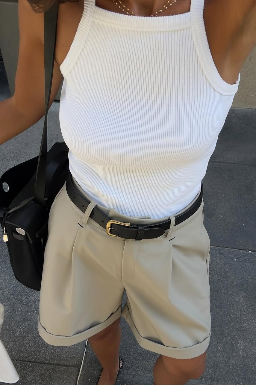 Chic summer outfit featuring a fitted white ribbed tank top paired with tailored beige long shorts and a black belt%2C perfect for casual outings