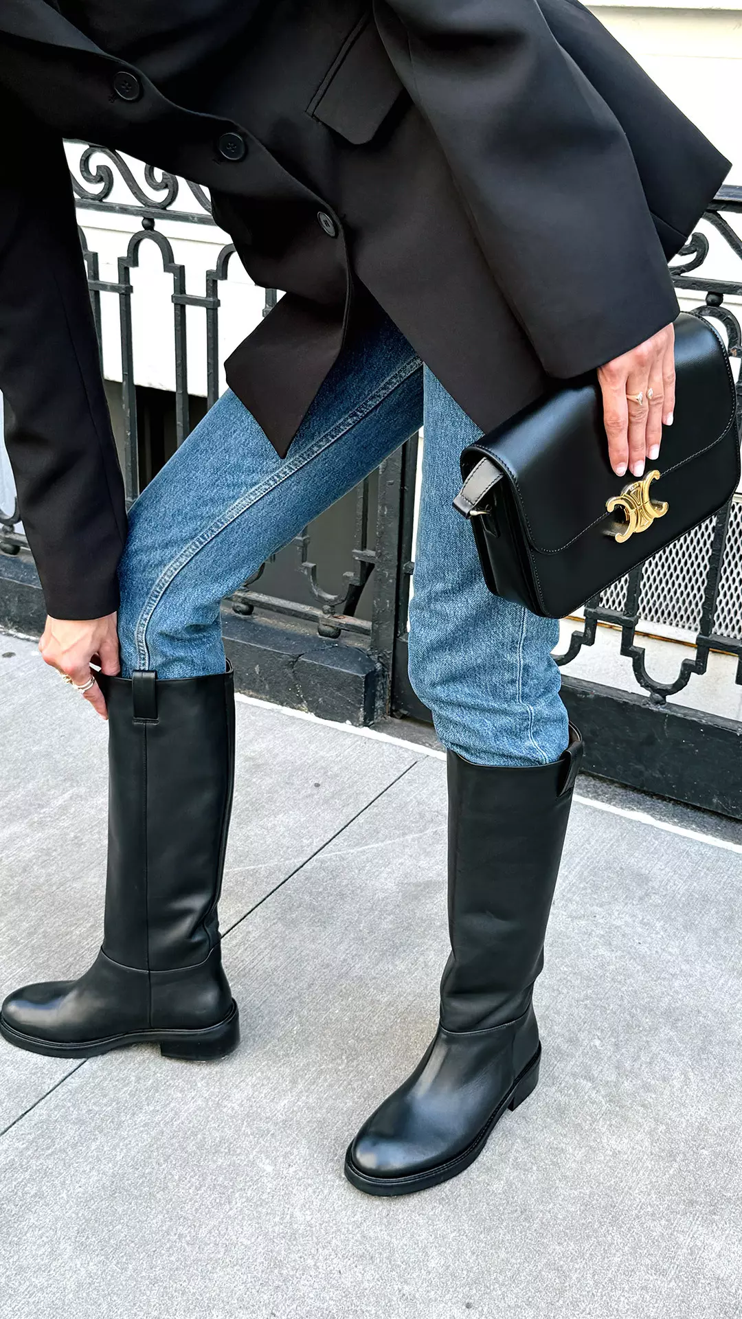 Sophisticated black riding boots with a sleek silhouette%2C paired with fitted blue jeans and a structured black handbag%2C perfect for transitional weather