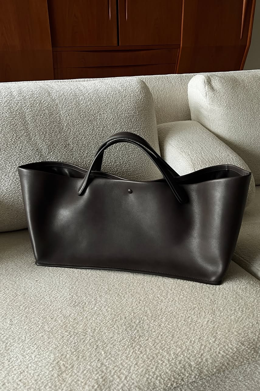 Minimalist black leather tote bag with elegant handles%2C perfect for weekend getaways or daily use%2C showcased on a soft textured surface