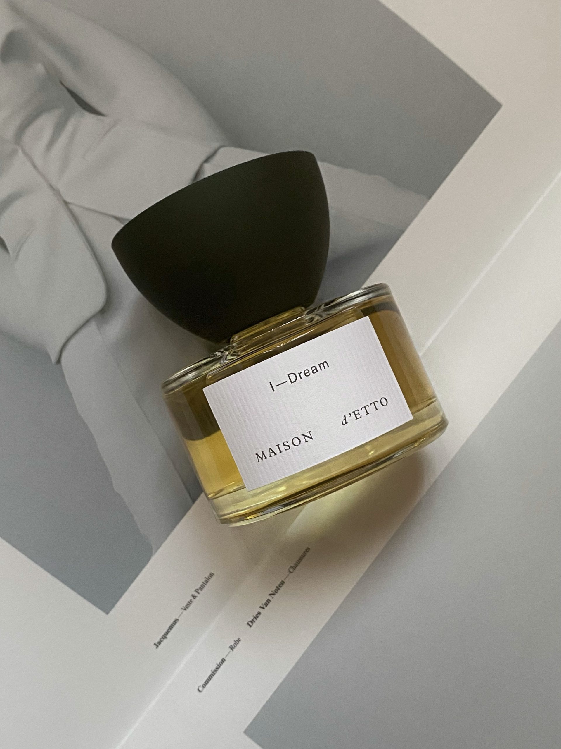 Maison d’Etto I–Dream perfume bottle with a sculptural dark cap styled on a minimalist grayscale editorial spread for an elevated flat lay look
