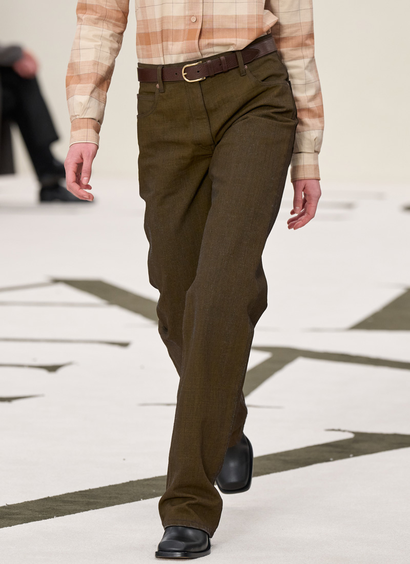Model wearing Calvin Klein brown wool trousers with plaid shirt and leather belt on minimalist runway