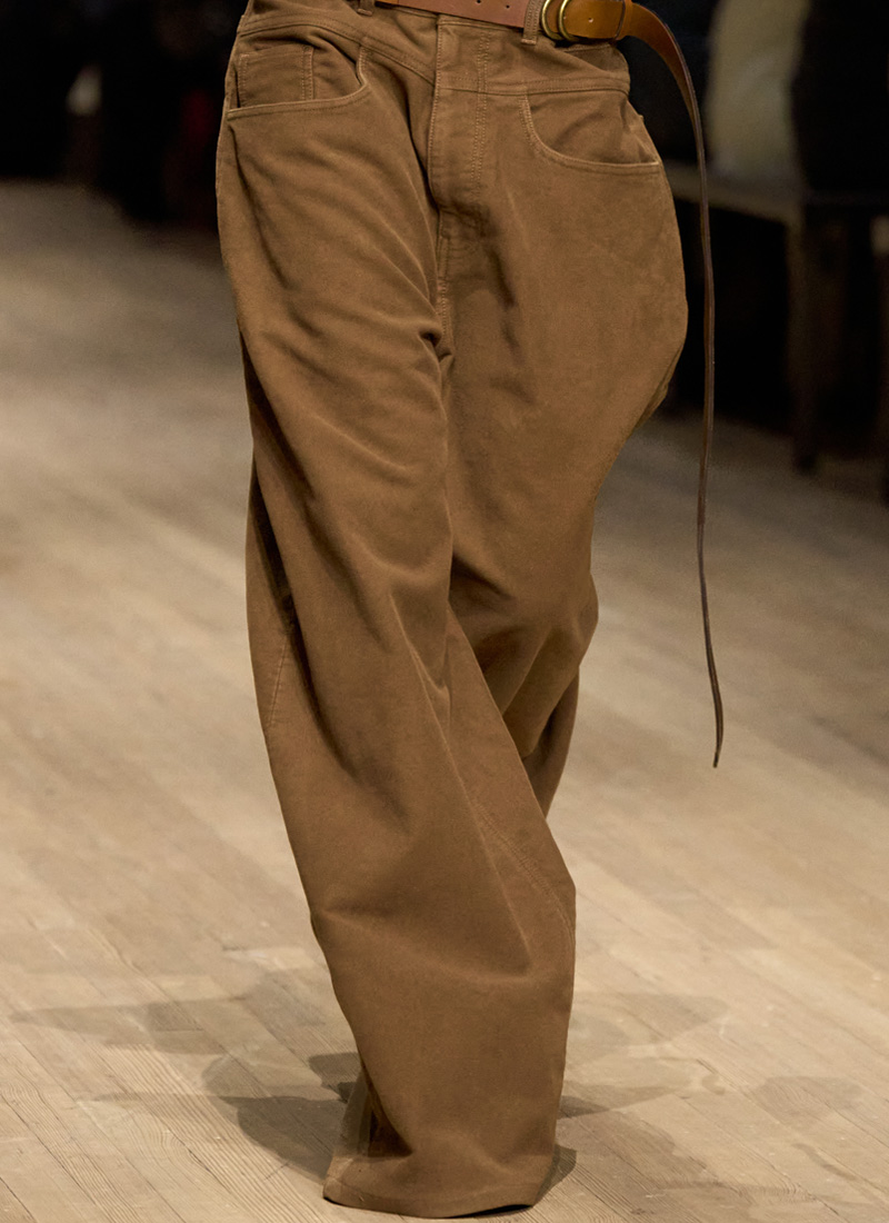 Model wearing Coach wide-leg brown corduroy pants with leather belt walking on wooden runway