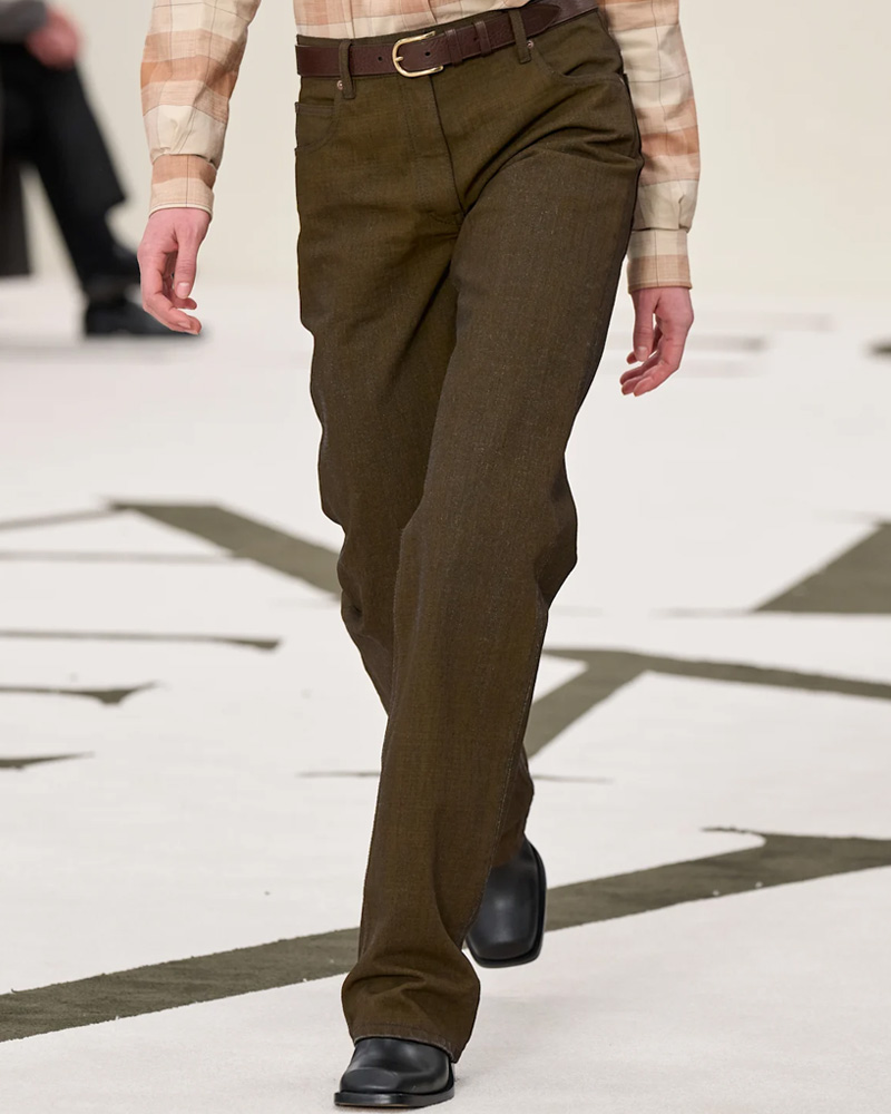 Model wearing Calvin Klein brown wool trousers with plaid shirt and leather belt on minimalist runway