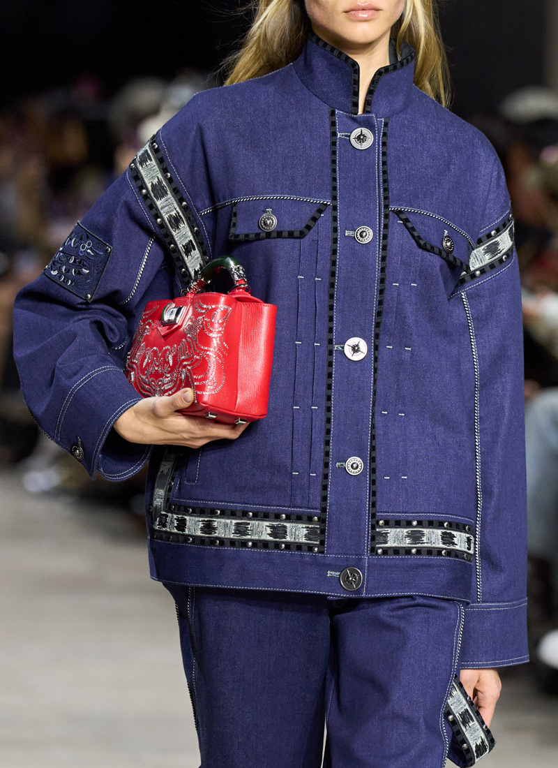 Model wearing Shiatzy Chen indigo denim jacket with silver trim and matching pants holding red bag