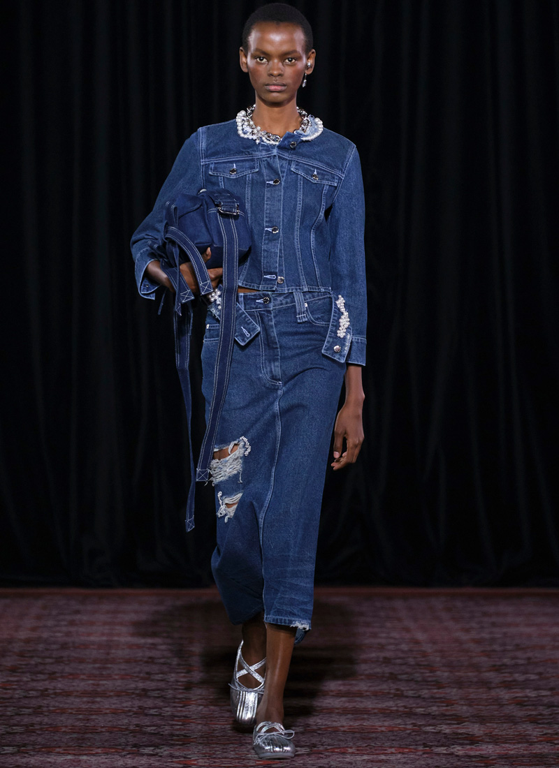 Model wearing Simone Rocha pearl-embellished denim jacket with ripped jeans and silver heels on runway