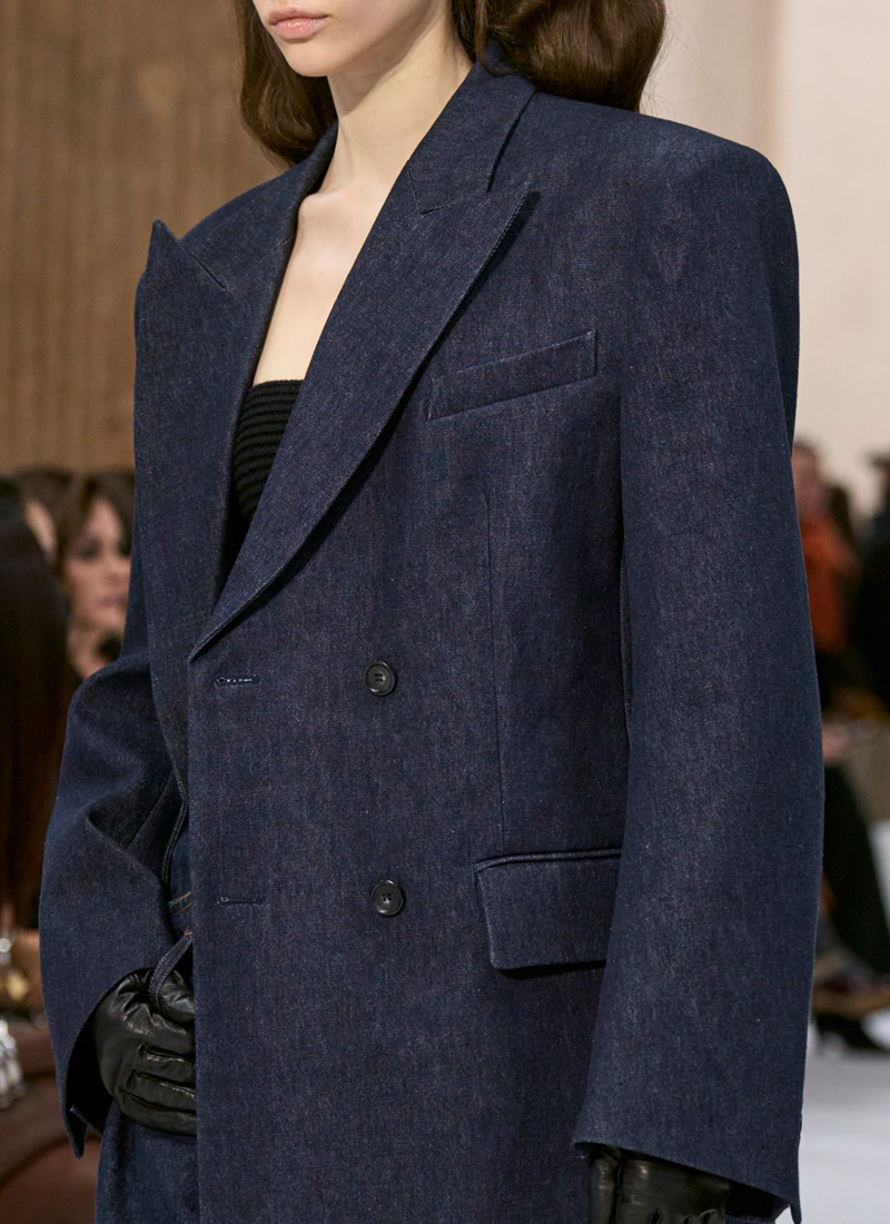 Model wearing structured blue double-breasted jacket with gathered waist and jeans on industrial runway