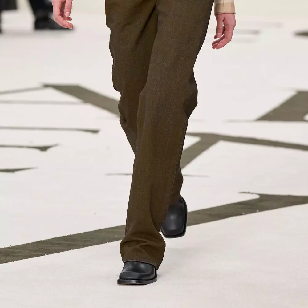 Model wearing Calvin Klein brown wool trousers with plaid shirt and leather belt on minimalist runway