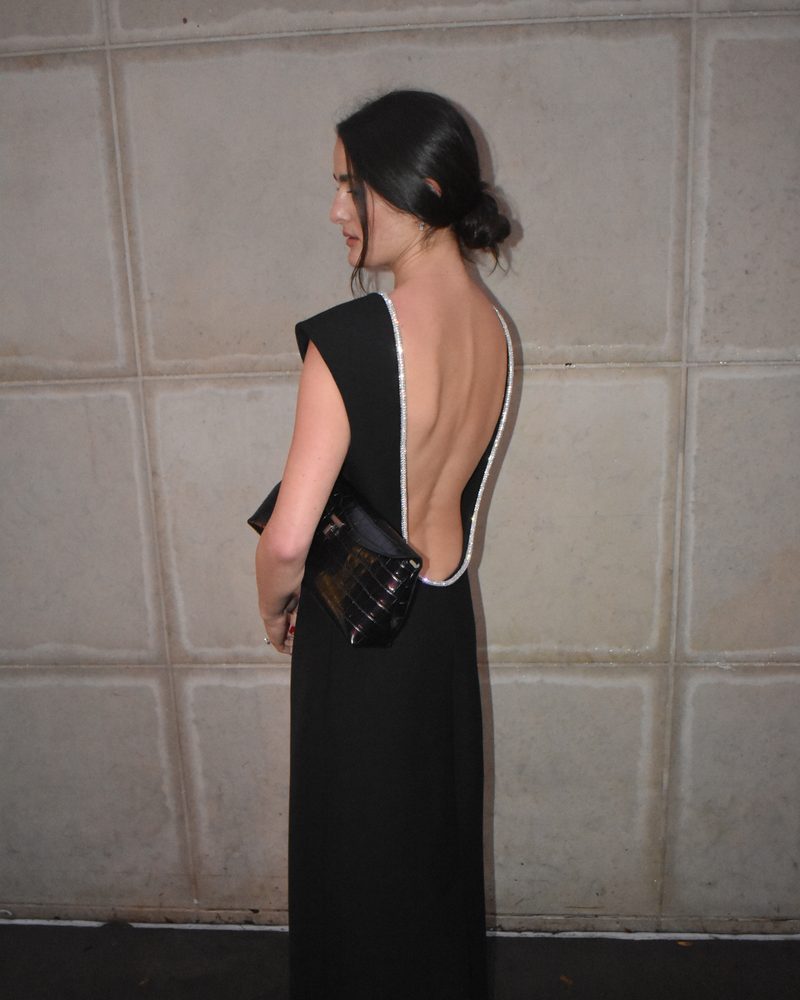 Sophisticated black evening gown featuring a plunging back and elegant silver detailing%2C paired with a sleek crocodile-embossed clutch