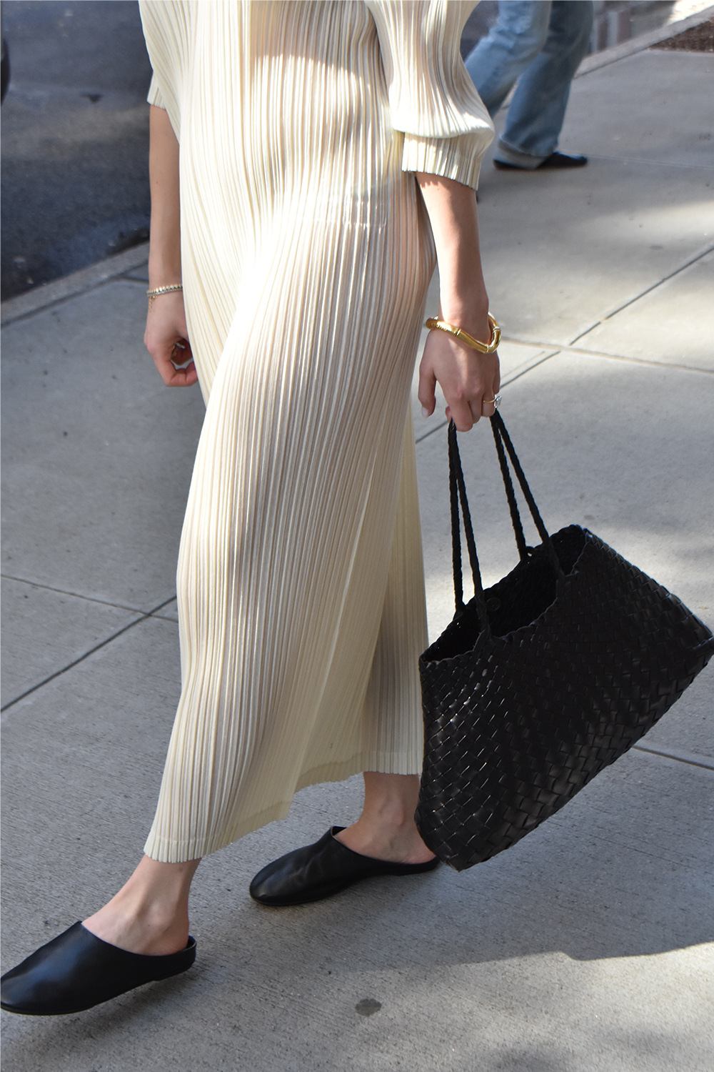 Elevated black leather house slippers paired with a stylish cream pleated dress and a woven black tote%2C enhancing chic%2C comfortable aesthetics