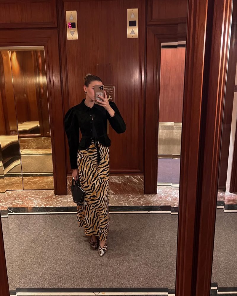 Stylish outfit featuring a black velvet blouse with puff sleeves%2C a tiger-striped skirt%2C and chic animal-print heels%2C complemented by a small black bag