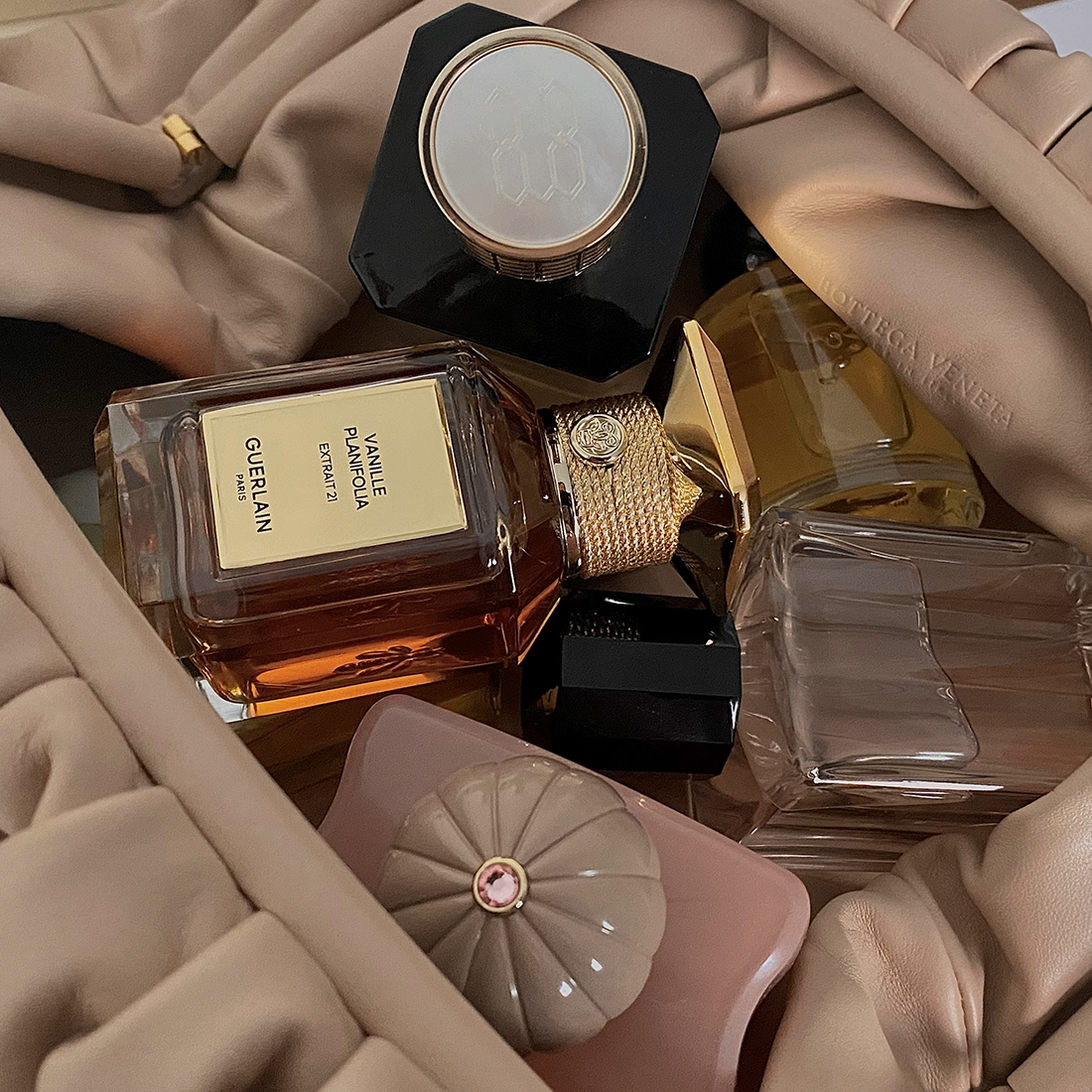 Elegant array of luxury perfume bottles, including Guerlain's Vanille Planguilla, nestled in a chic Bottega Veneta bag