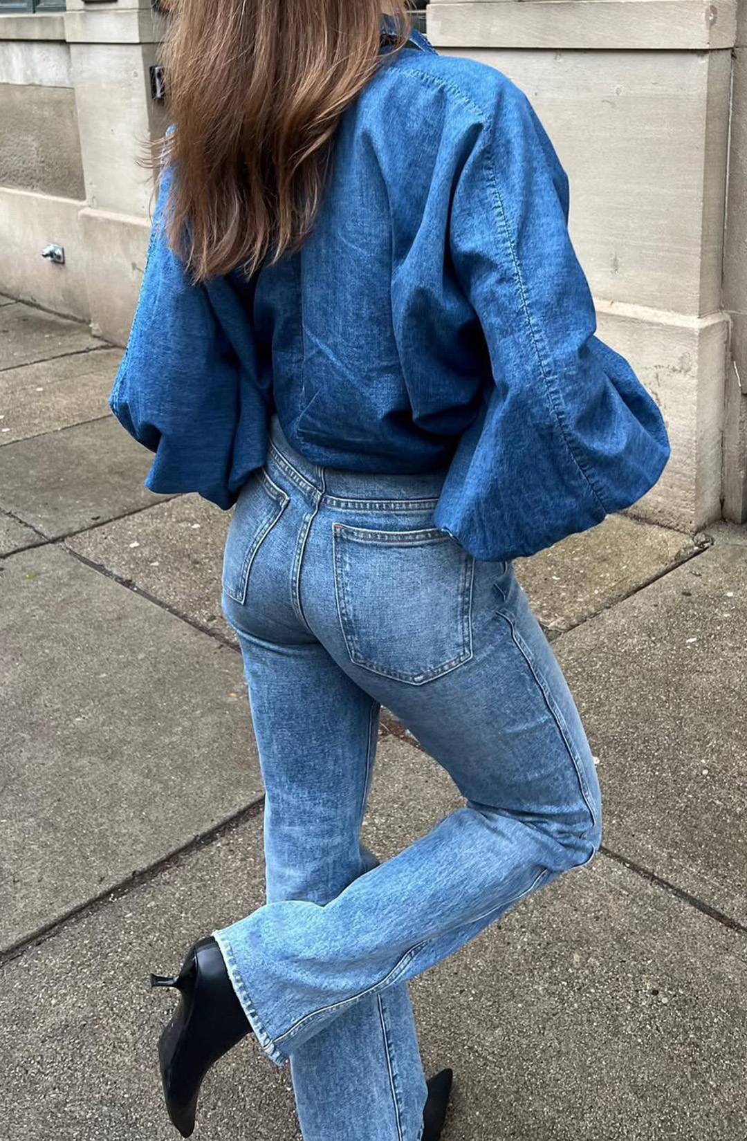 Woman wearing a denim-on-denim outfit with balloon-sleeve shirt%2C high-rise jeans%2C and black ankle boots on city street