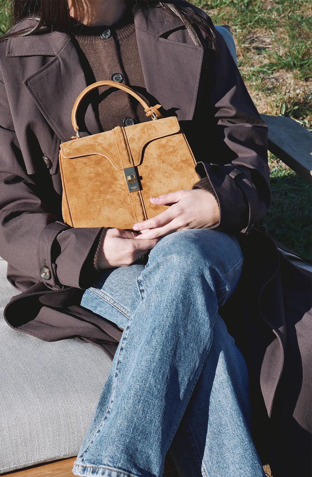 Chic spring outfit featuring a stylish taupe suede handbag with a structured shape%2C paired with a cozy brown sweater and denim jeans