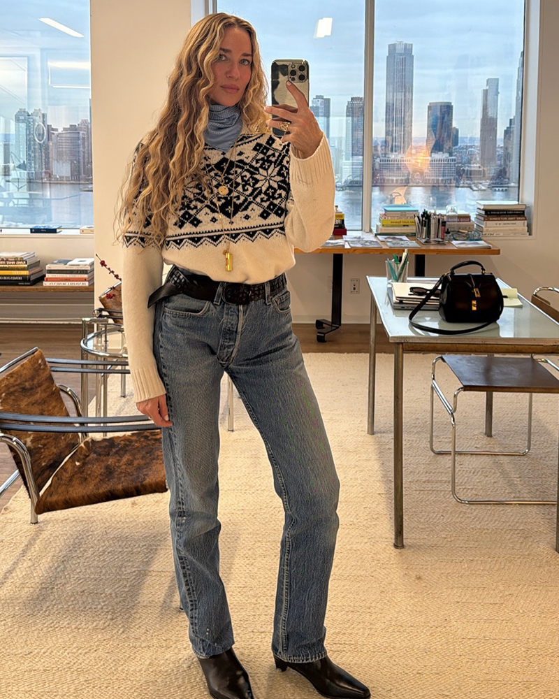 Mirror selfie of a blonde wearing a Nordic-pattern knit sweater%2C straight-leg jeans and boots%2C styled in a city-view office