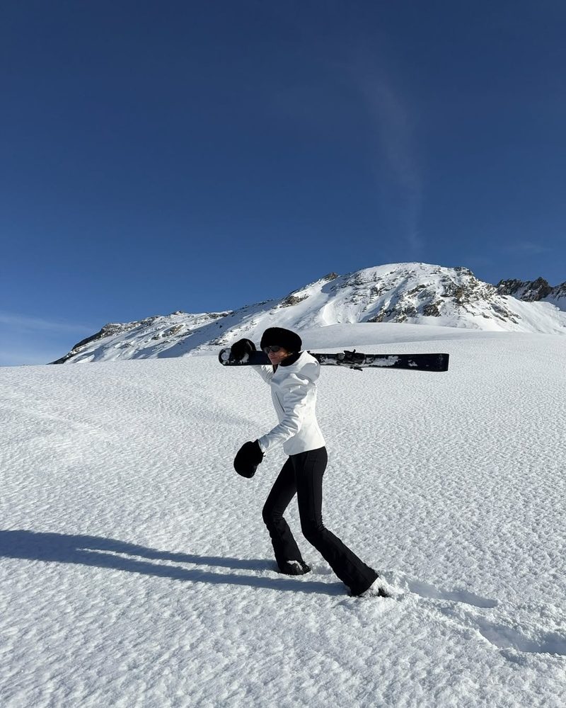 Sleek white ski jacket paired with fitted black ski pants%2C accessorized with a black beanie and gloves%2C set against snowy alpine backdrop